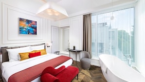 Quarto de hotel moderno com uma cama grande, área de estar, banheira e vista para a cidade.