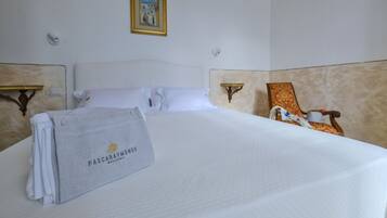 Uma cama bem arrumada com uma toalha e um roupão, uma cadeira com uma almofada estampada e um quadro na parede.