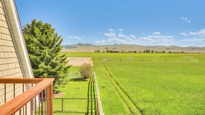 Vista de uma varanda com vista para um campo verde e uma cordilheira ao fundo.