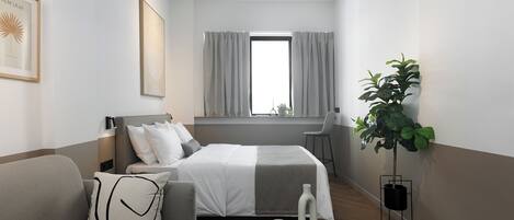 Quarto de hotel moderno com cama, sofá, mesa de jantar e um vaso de planta.