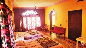 Quarto com cama, sofá vermelho, cadeira e janela com cortinas florais.