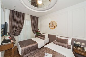 Quarto de hotel com duas camas, uma escrivaninha com computador, telefone e uma mesinha com um vaso de flores.