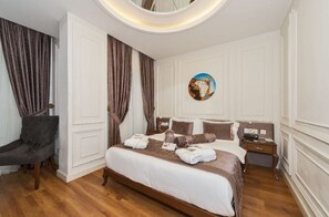 Quarto de hotel com uma cama grande, uma cadeira, uma mesa de cabeceira e um quadro redondo na parede.