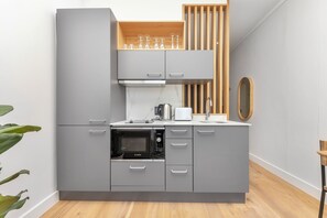 Cozinha compacta com armários cinzas, micro-ondas, chaleira e cafeteira.