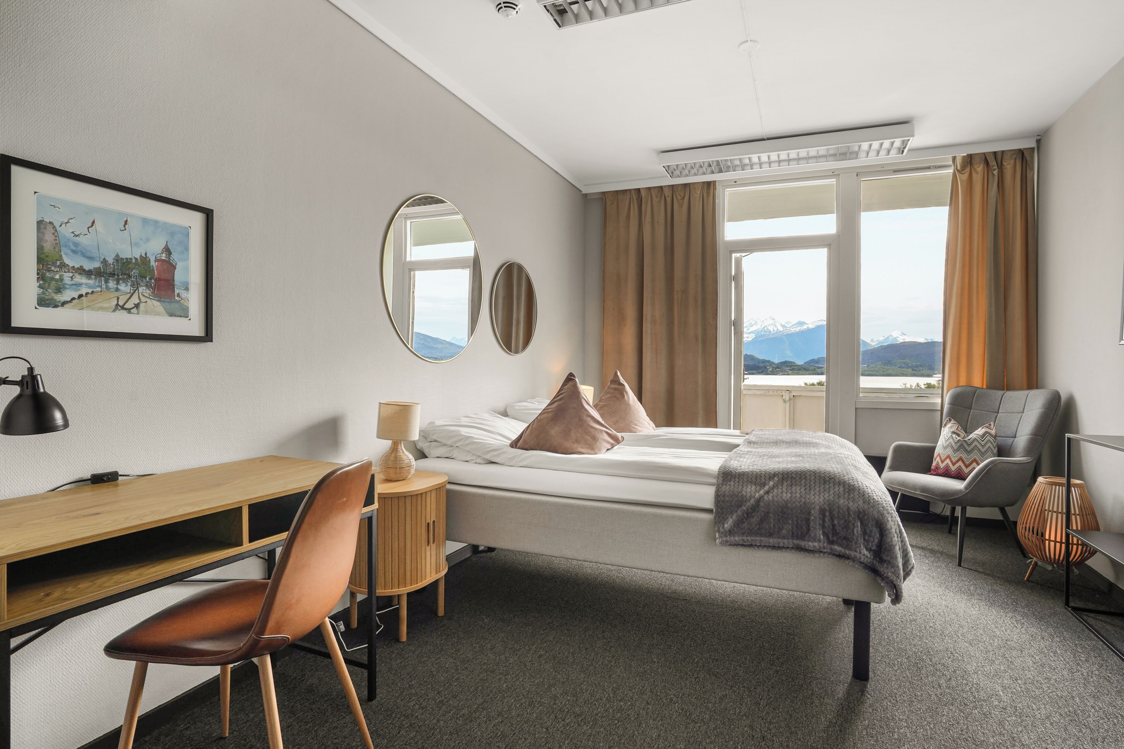 Quarto de hotel com cama, escrivaninha, cadeira e uma grande janela com vista.