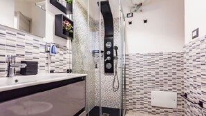 Casa de banho moderna com chuveiro envolto em vidro, um lavatório grande e uma sanita.