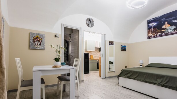 Quarto com cama, mesa de jantar com cadeiras, pequena cozinha e banheiro visível por uma porta aberta.