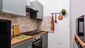 Cozinha compacta com bancada de madeira, fogão e pia. Há armários, micro-ondas e uma pequena planta em vaso na parede.