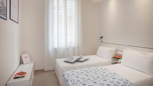 Quarto com duas camas, uma mesinha de cabeceira com livros, uma cortina e um lustre.
