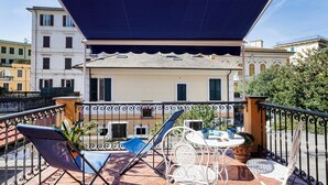 Um terraço com móveis de exterior, uma pérgula e vista para um edifício com várias janelas e varandas.