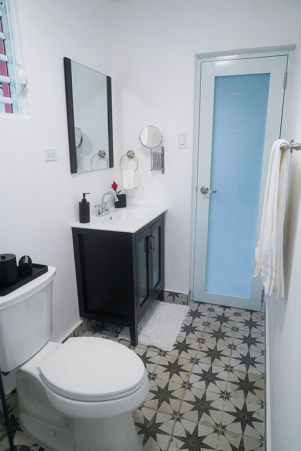 Um banheiro com vaso sanitário branco, pia com espelho e porta azul.