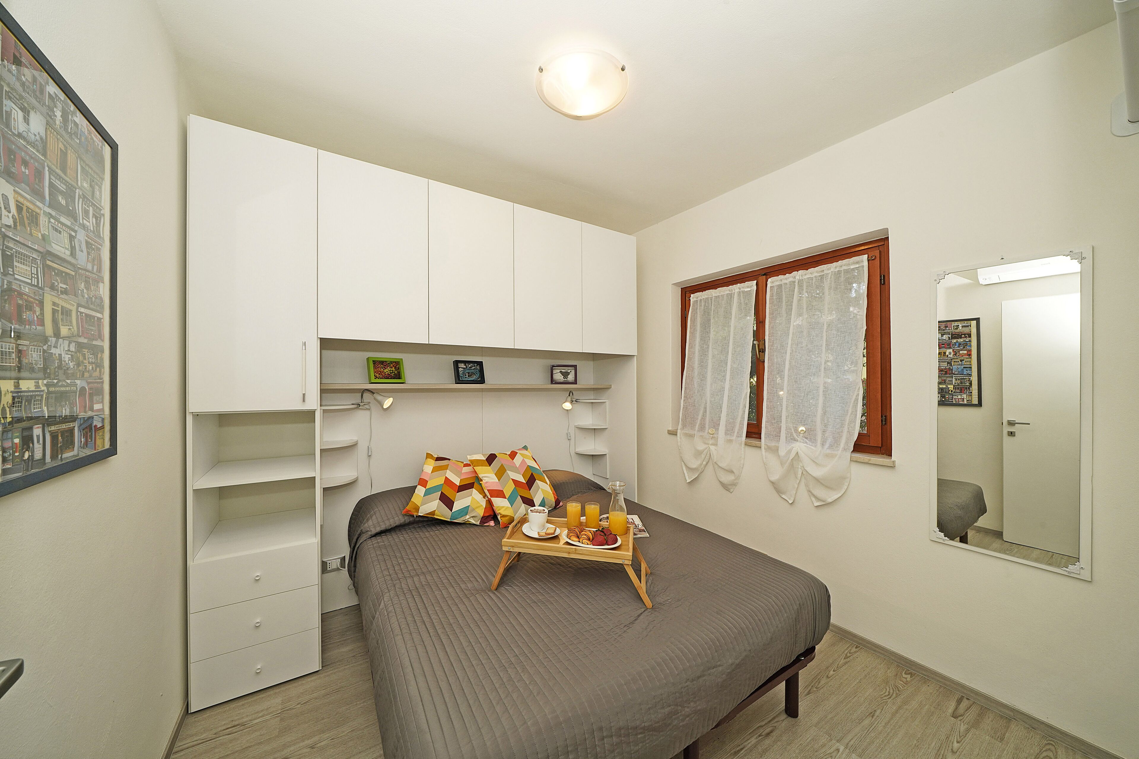 Quarto com cama, mesa de cabeceira com bandeja de café da manhã, guarda-roupa, janela com cortinas e espelho.