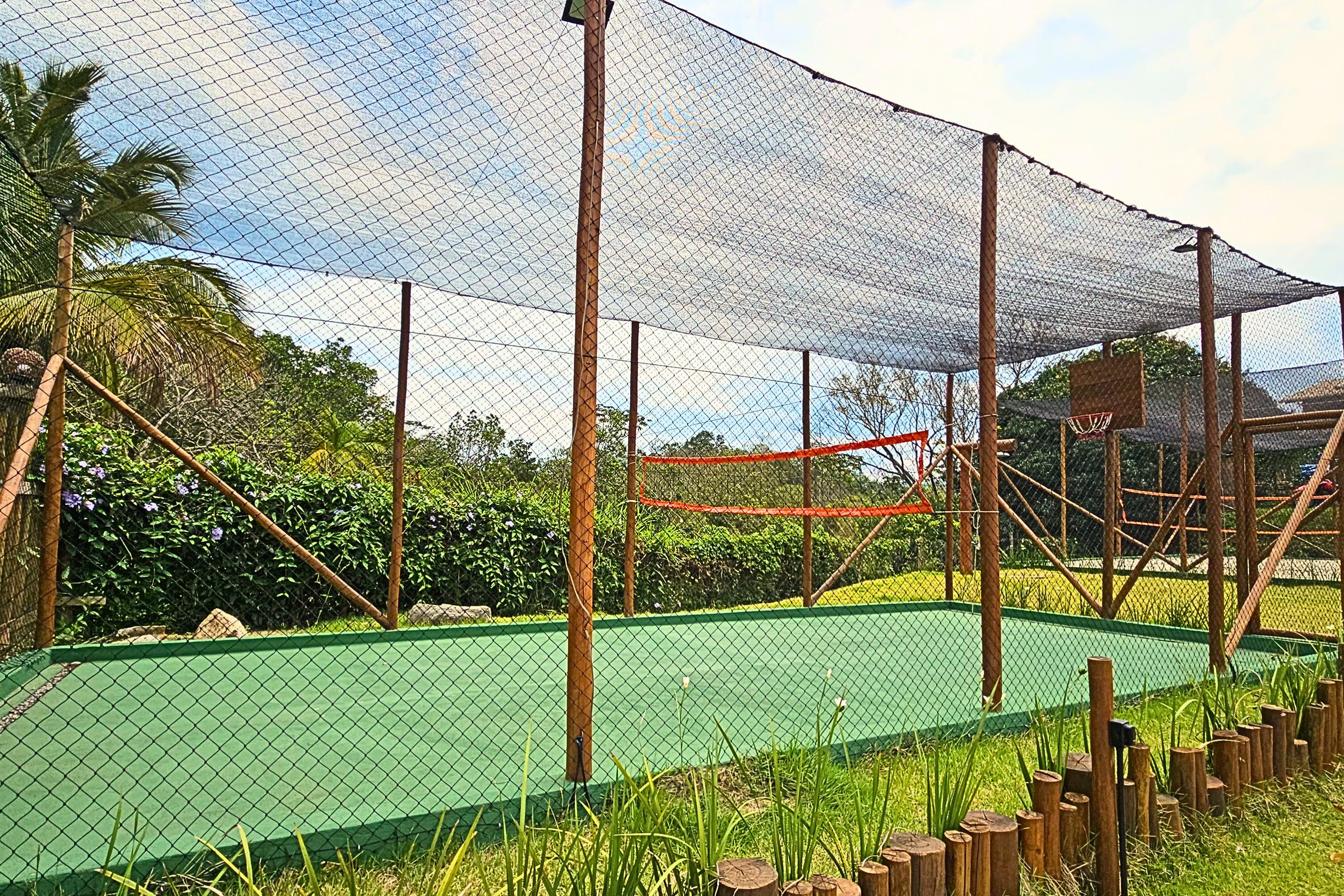 Uma quadra de basquete cercada por uma cerca de rede, rodeada por vegetação e árvores.