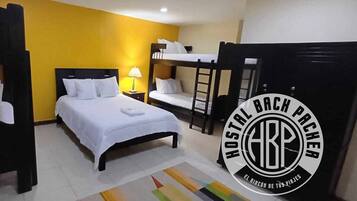 Quarto de hotel com beliches, mesa de cabeceira com abajur e tapete colorido.