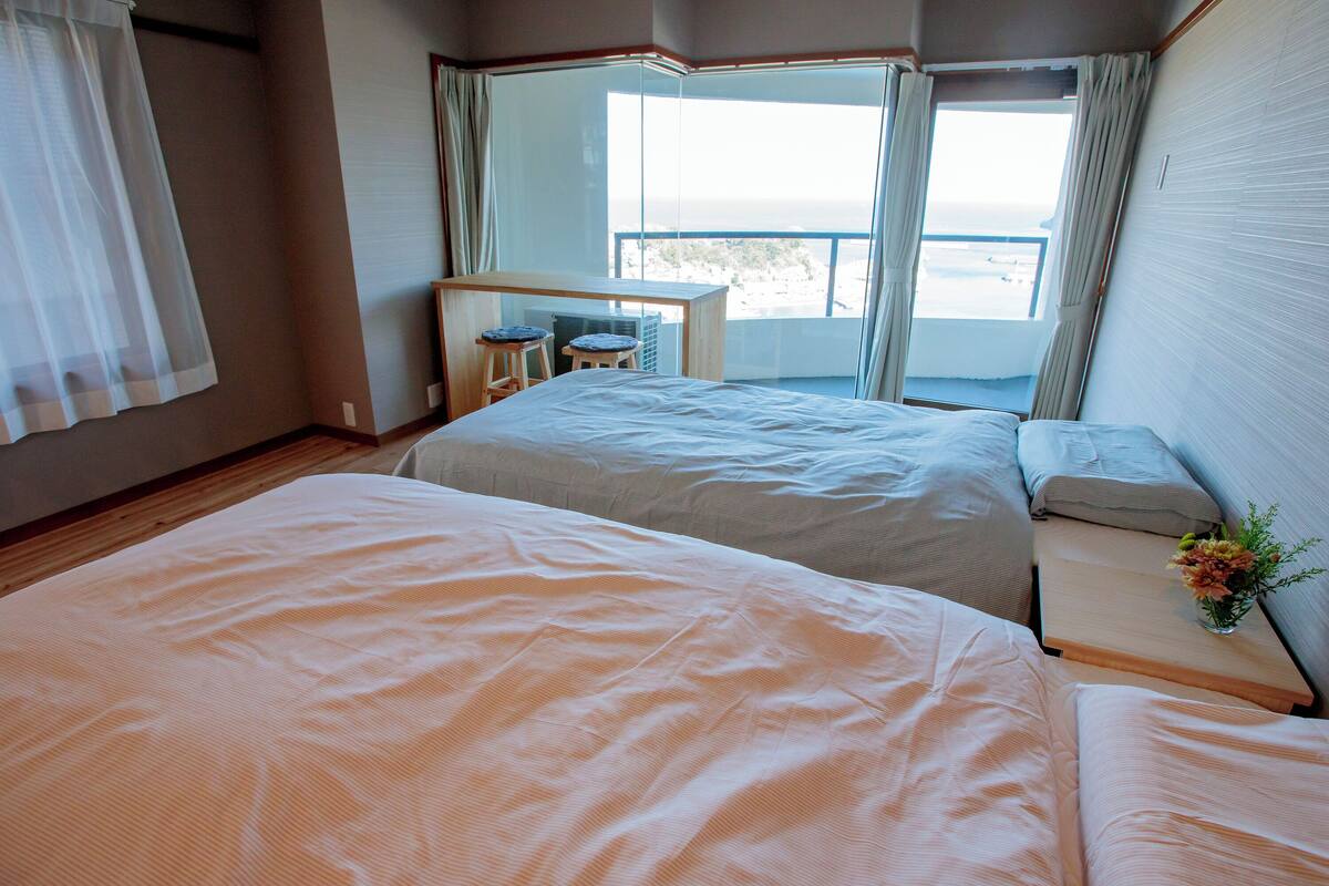 Quarto de hotel com duas camas, uma mesa e vista para a praia.