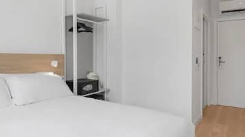 Quarto de hotel com cama, armário, mesa de cabeceira e ar condicionado.