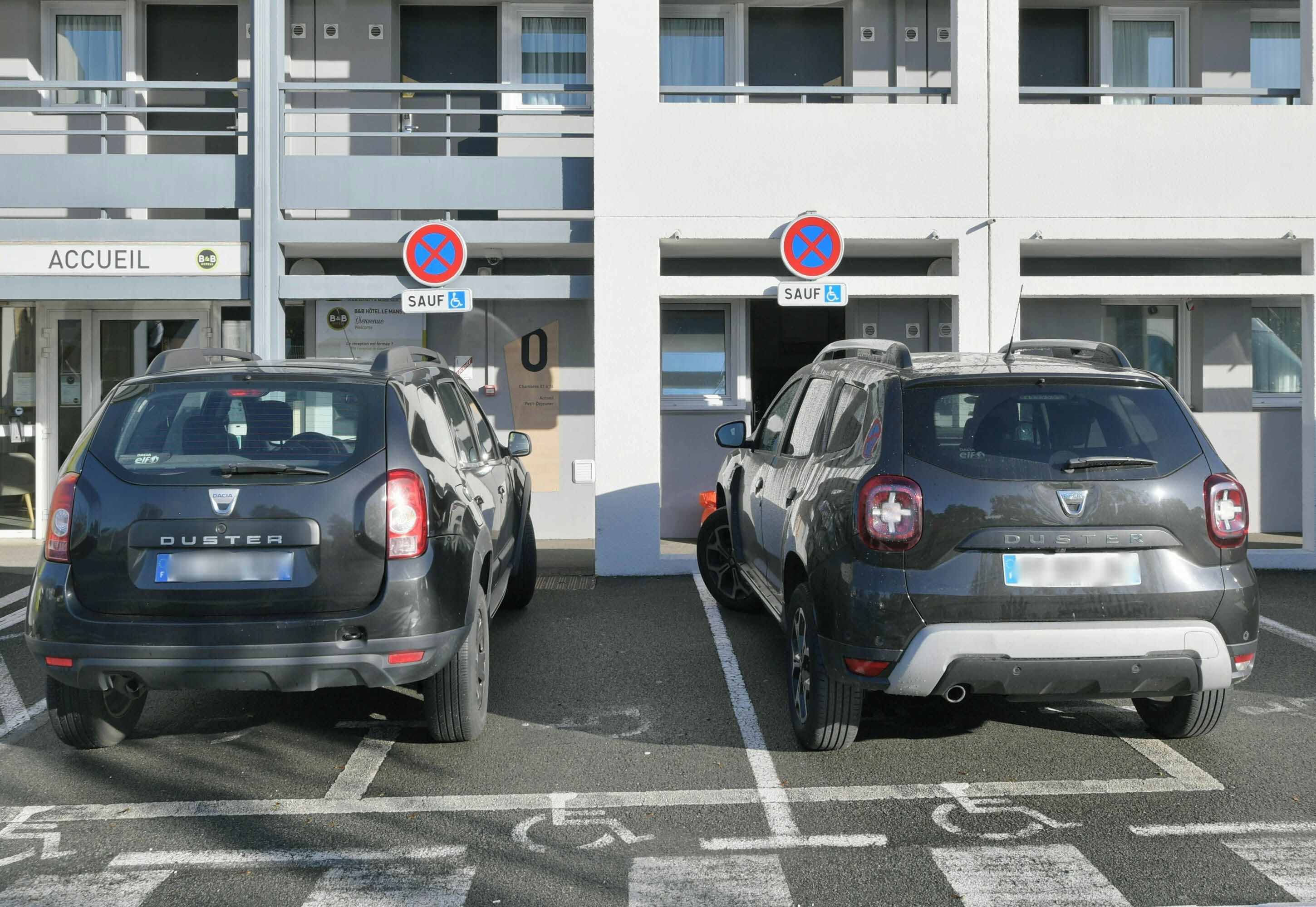 Dois carros Duster estacionados num parque de estacionamento, com um edifício com a inscrição 'ACCUEIL' ao fundo.