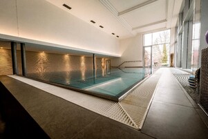 Piscina interior moderna com parede de vidro, parede texturizada em um lado e ampla vista para o exterior através de grandes janelas.