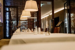 Uma sala de jantar com uma mesa comprida posta para refeição, com luminárias pendentes e uma parede texturizada ao fundo.