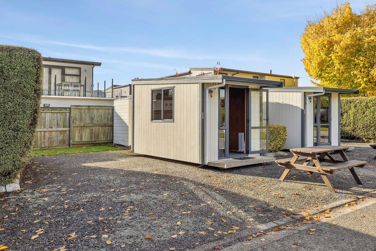 Uma casa móvel compacta, térrea, com um pequeno alpendre e uma mesa para piquenique.