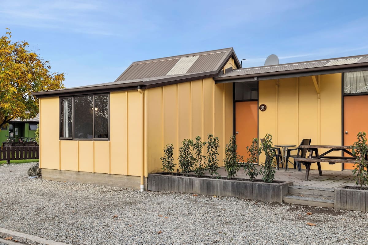 Um edifício amarelo com um pequeno alpendre, um banco de madeira e uma porta com o número 31.