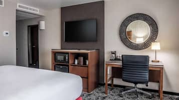Quarto de hotel com cama, escrivaninha e cadeira, televisão, máquina de café, micro-ondas e um espelho grande.