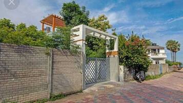 Área residencial murada, com muro de tijolos, pérgola de madeira e portão branco.