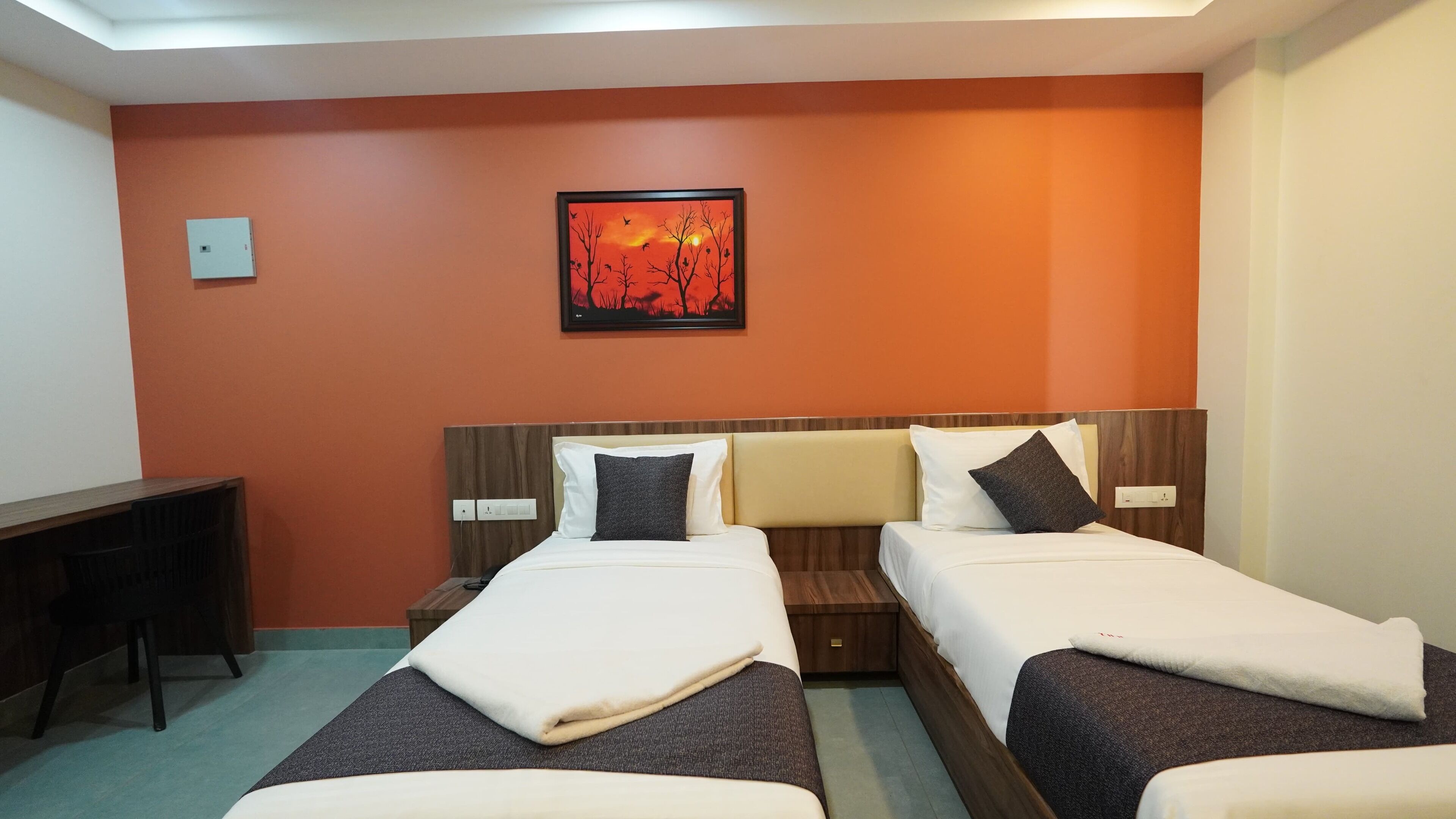 Quarto de hotel com duas camas, uma escrivaninha e um quadro na parede.