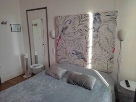 Quarto com cama, almofadas, luminária na parede, espelho e radiador.