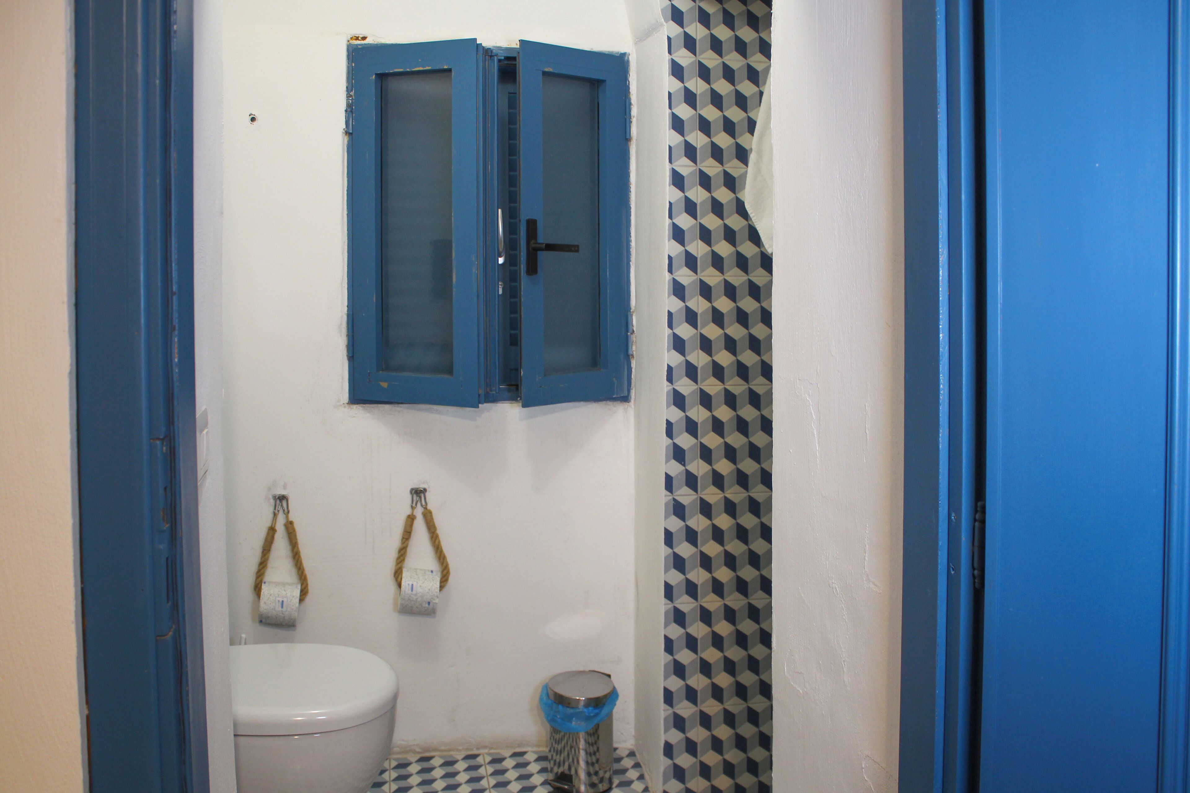 Um banheiro com vaso sanitário, um armário azul e cortina de chuveiro estampada.