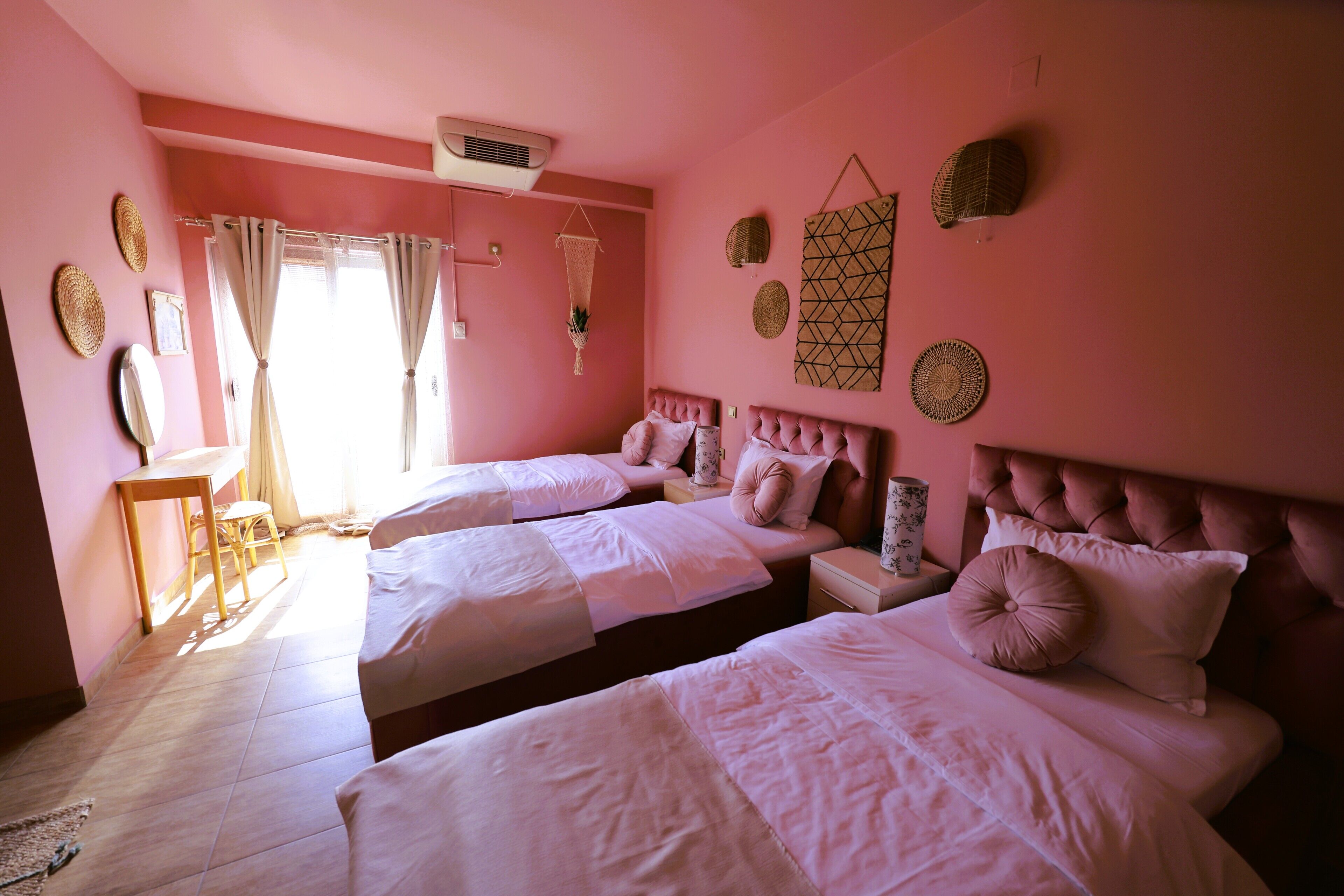 Quarto decorado em tons de rosa, com duas camas, uma escrivaninha e elementos decorativos nas paredes.