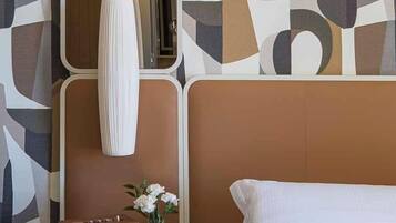 Quarto de hotel com design moderno, apresentando um espelho grande, mesa de cabeceira com abajur, rádio e um vaso com flores.