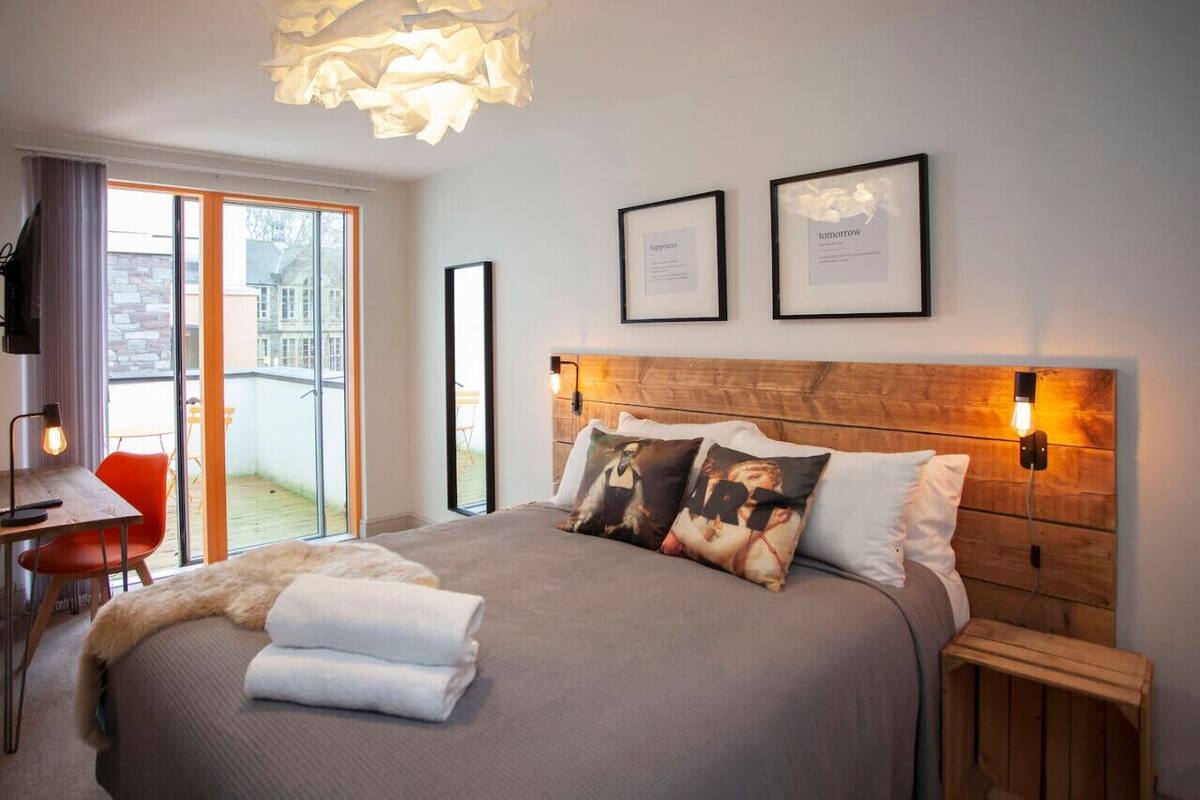 Quarto de hotel moderno com uma cama grande, cabeceira de madeira e dois certificados emoldurados na parede.