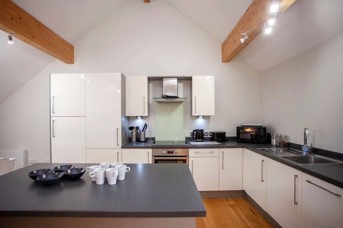 Uma cozinha moderna com armários brancos, uma ilha central com tigelas e canecas, um fogão e um micro-ondas.