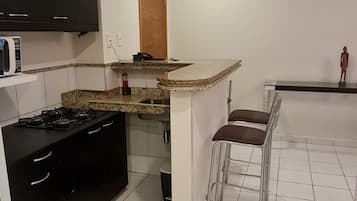 Cozinha compacta com micro-ondas, fogão e banquetas.