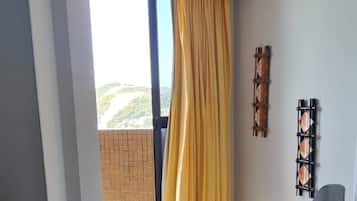 Quarto com porta de correr de vidro, sofá preto, luminária pendente e prateleira fixada na parede.