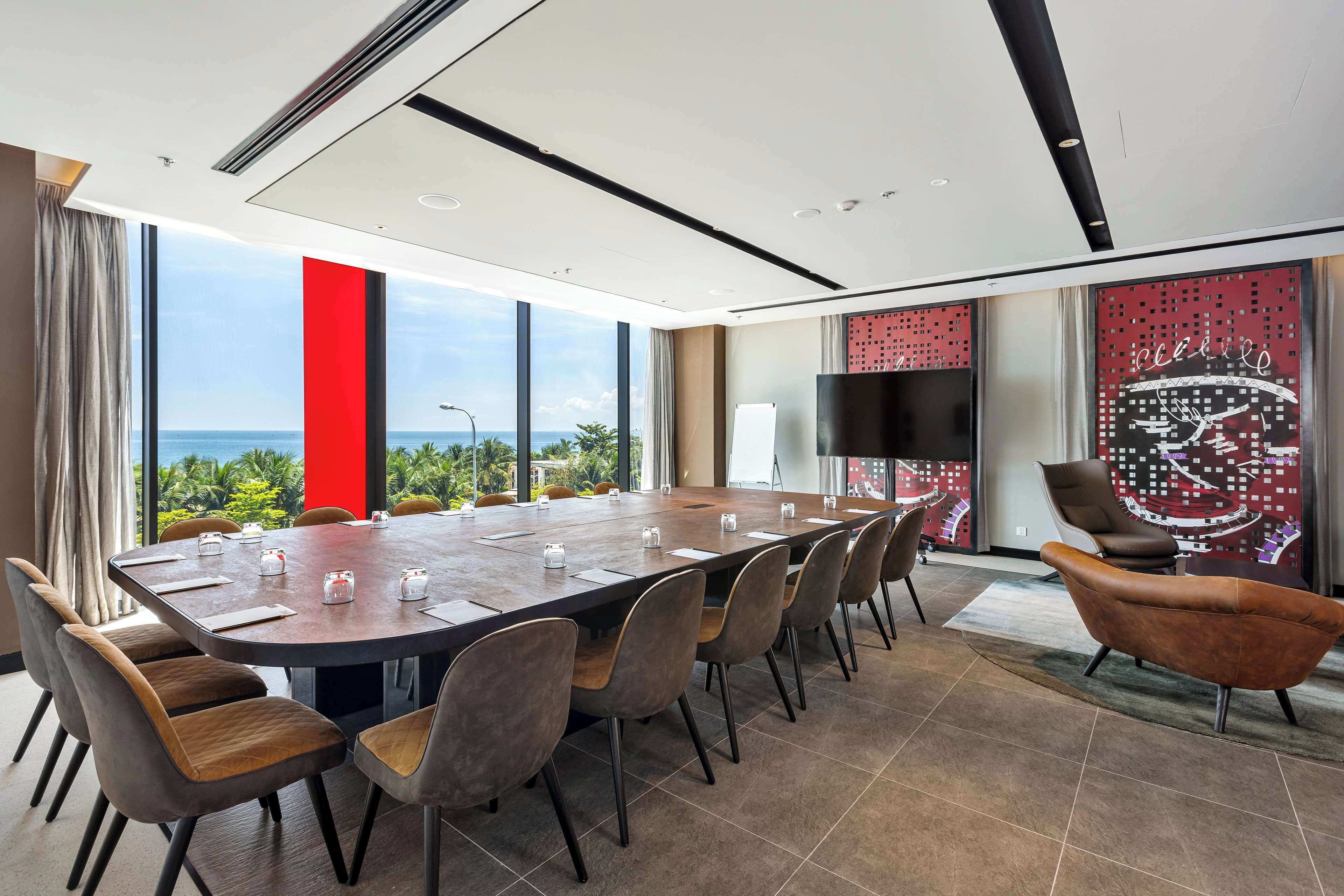 Uma sala de conferências moderna com uma mesa grande, cadeiras confortáveis, uma janela ampla com vista para o oceano e uma tela digital na parede.