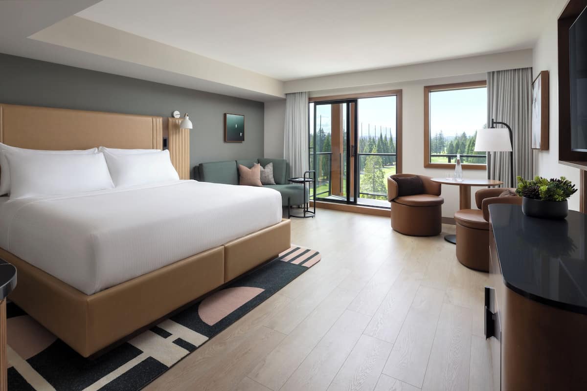 Quarto de hotel moderno com uma cama grande, varanda com vista, mesa pequena e área de estar.