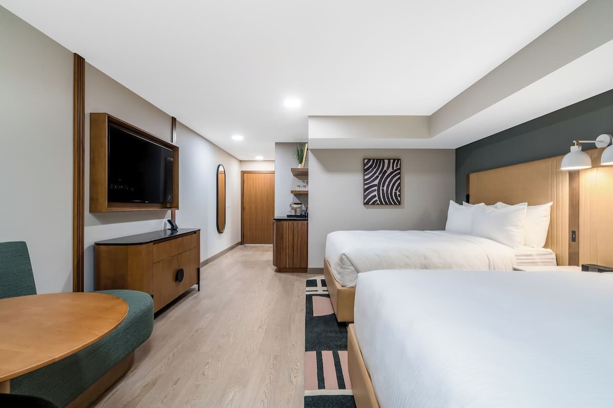 Quarto de hotel moderno com escrivaninha de madeira, televisão de tela plana, cama com lençóis brancos e uma obra de arte com padrão de zebra na parede.