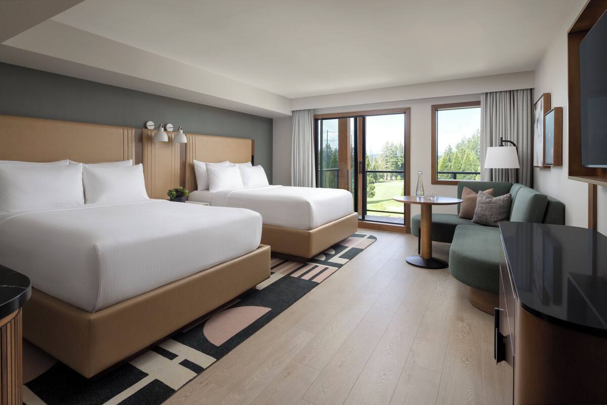 Quarto de hotel com duas camas, um sofá, uma TV e uma varanda com vista.
