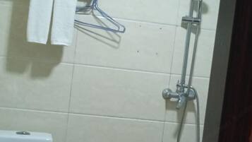 Uma casa de banho com sanita, suporte de toalhas e chuveiro.