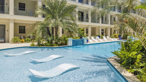 Uma área de piscina de hotel com vários níveis, palmeiras e espreguiçadeiras.