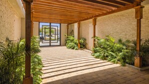 Uma área externa coberta com piso de tijolos, vigas de madeira e plantas em vasos.