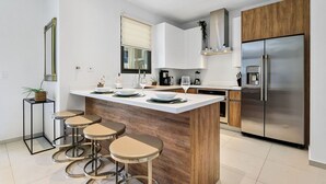 Uma cozinha moderna com uma ilha central, banquetas, geladeira e armários de madeira.