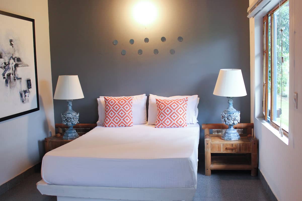 Cama bem arrumada com almofadas estampadas em branco e laranja, duas luminárias de mesa e um ponto de luz fixado na parede.