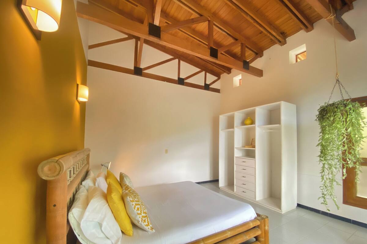 Quarto com cama de madeira, paredes brancas e guarda-roupa branco.
