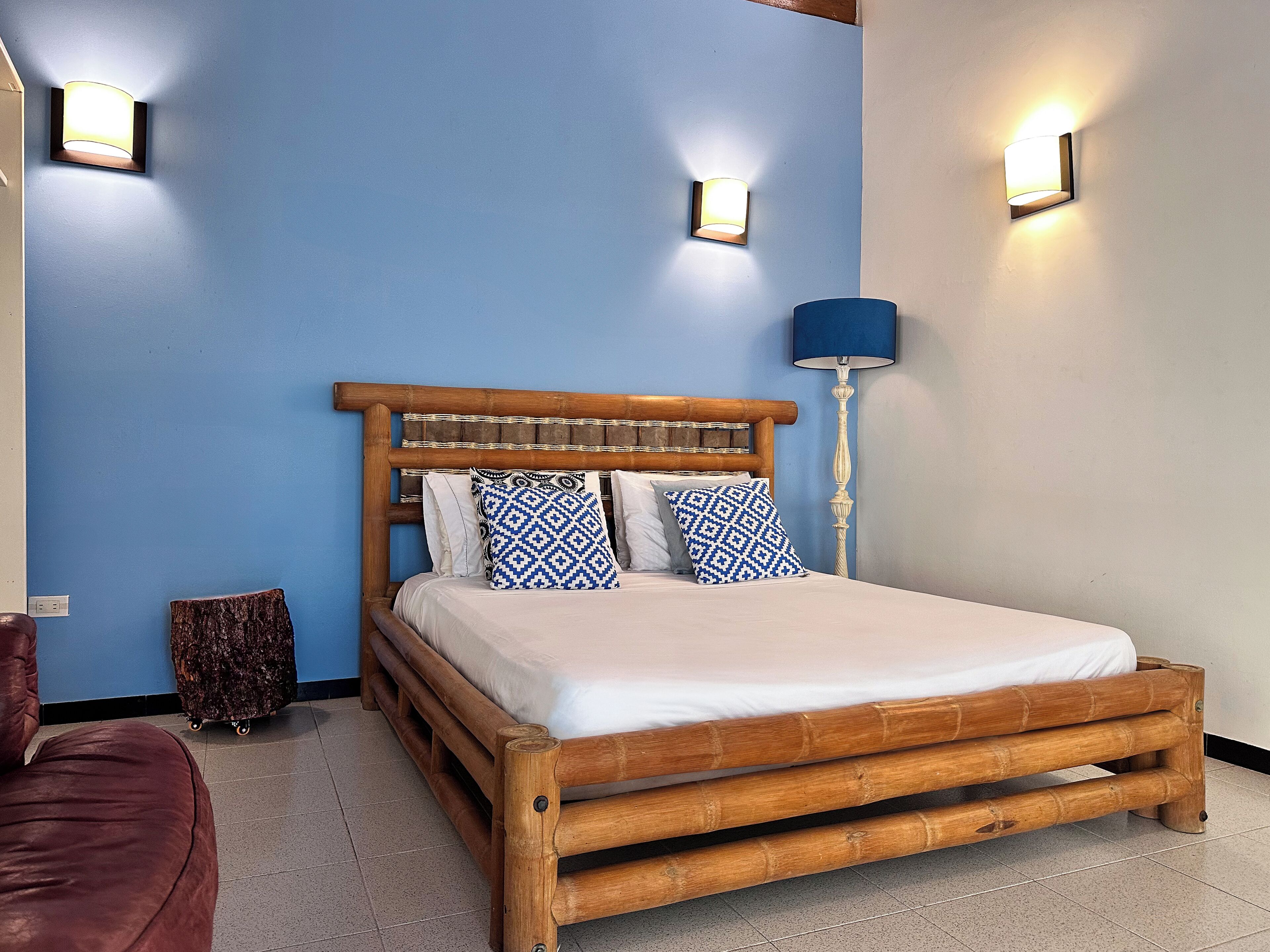 Uma cama com estrutura de madeira, duas almofadas, um abajur e uma luminária na parede.