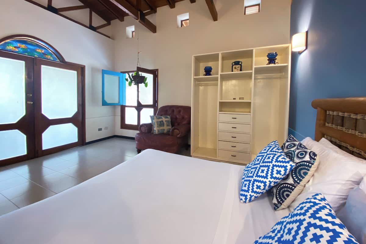 Quarto com uma cama grande, guarda-roupa, cadeira e planta pendente.