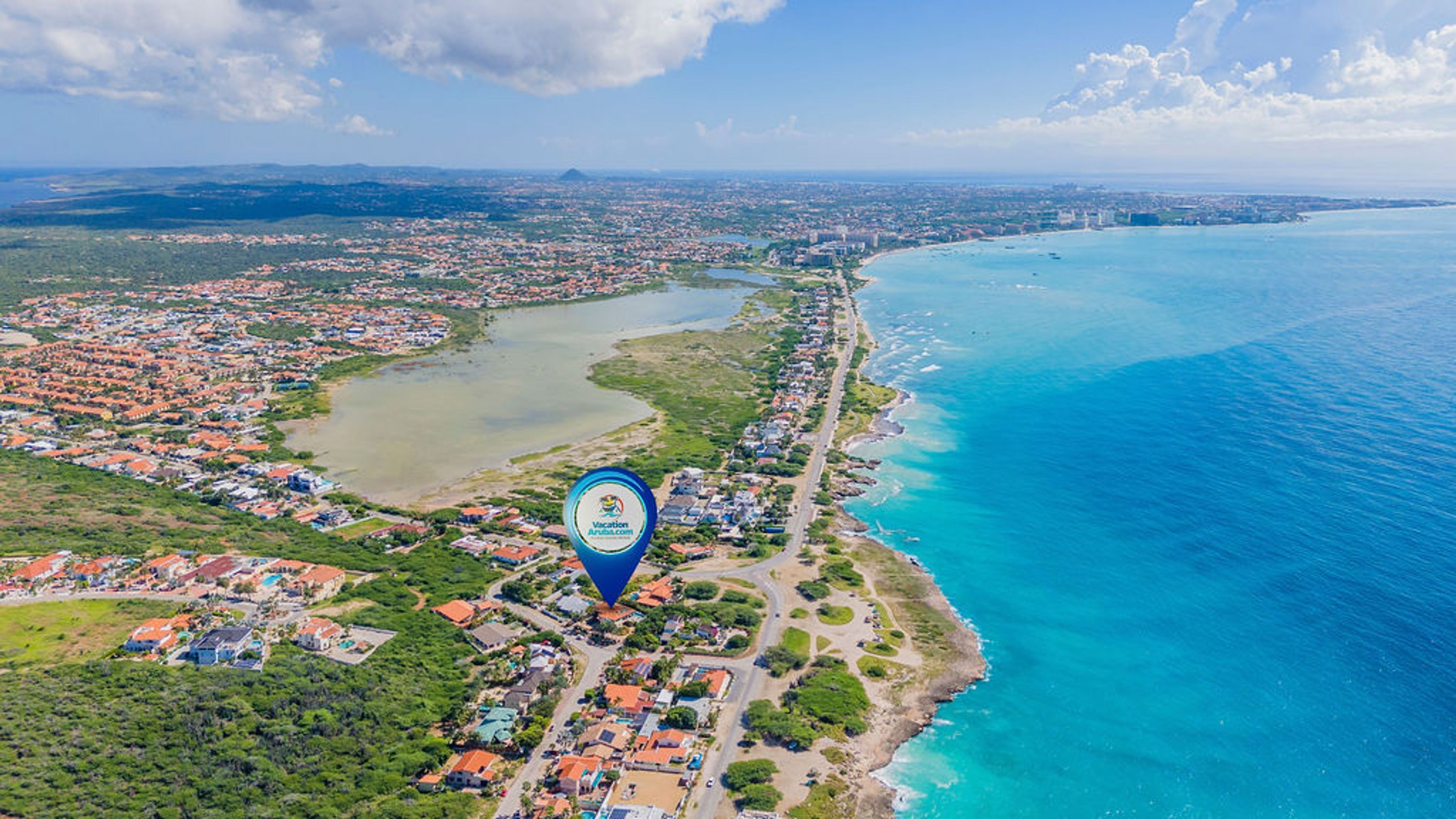 Vista aérea de uma cidade costeira com edifícios residenciais e comerciais, um porto de iates e um mar azul límpido.