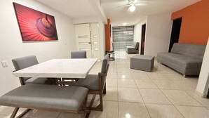 Uma sala de estar moderna com uma mesa de jantar, sofás cinza e uma grande pintura abstrata na parede.